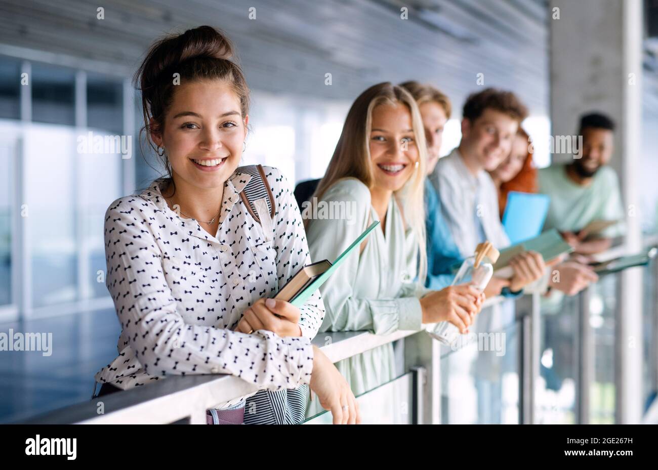 University students standing and looking at camera indoors, back to ...