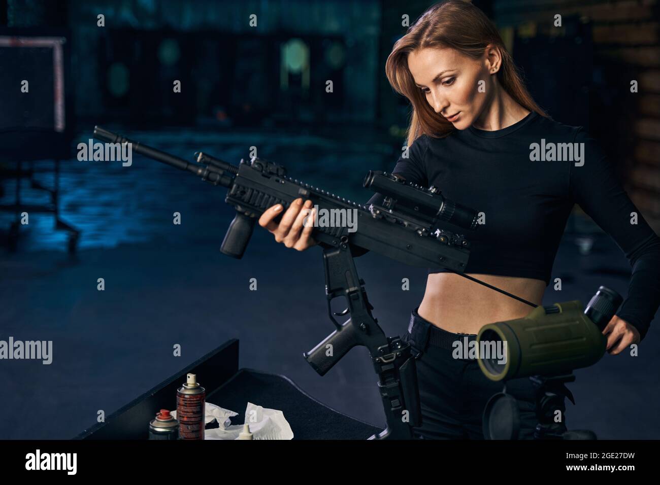 Concentrated experienced female shooter cleaning her assault rifle ...