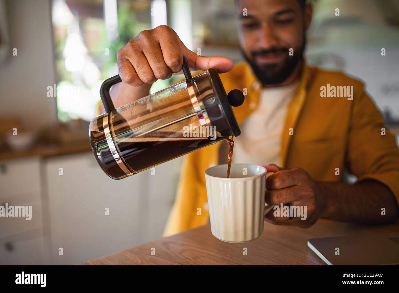 Young man pouring coffee from french press working indoors, home office ...
