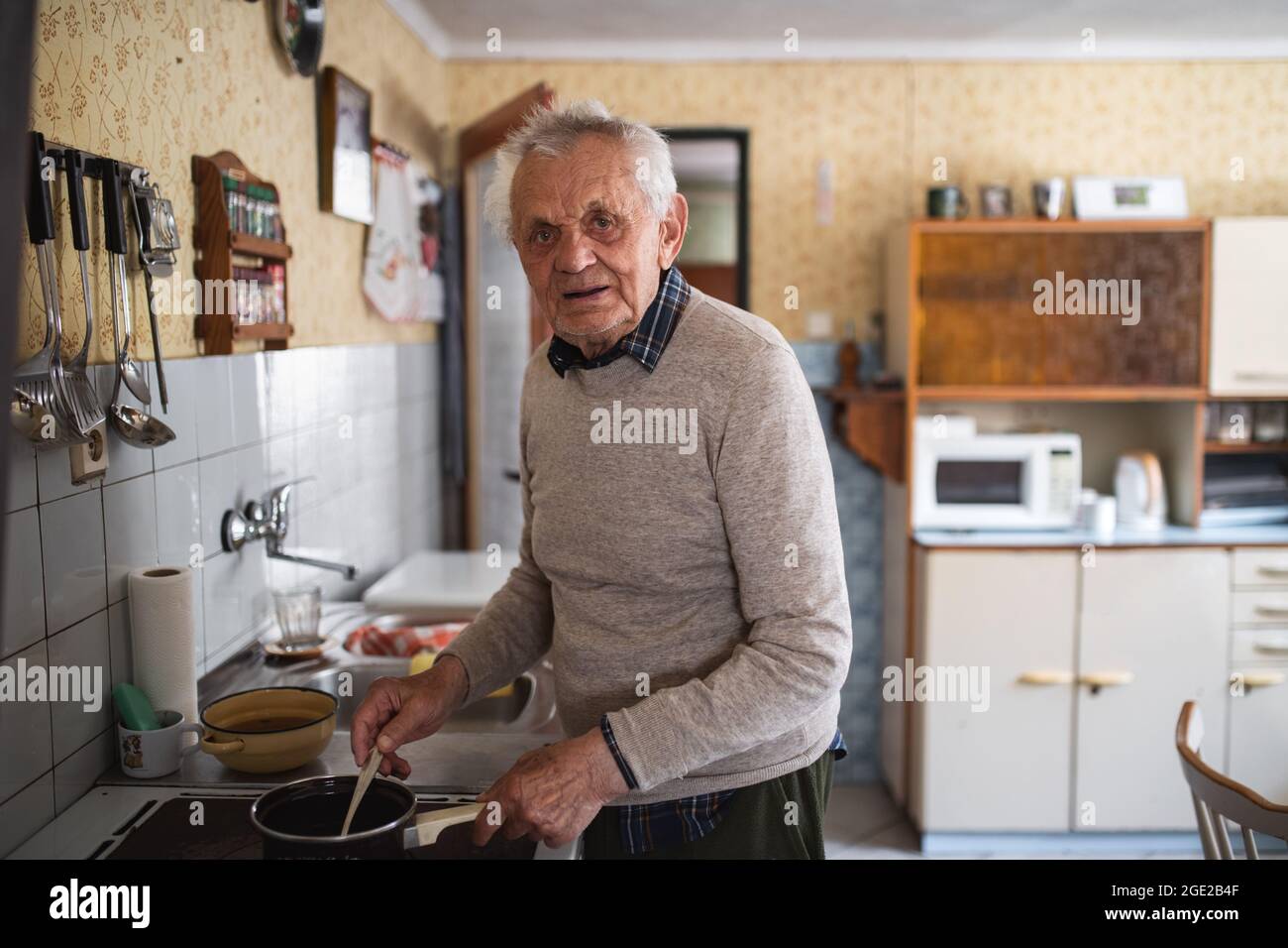Portrait of elderly man cooking on stove indoors at home, stirring and ...