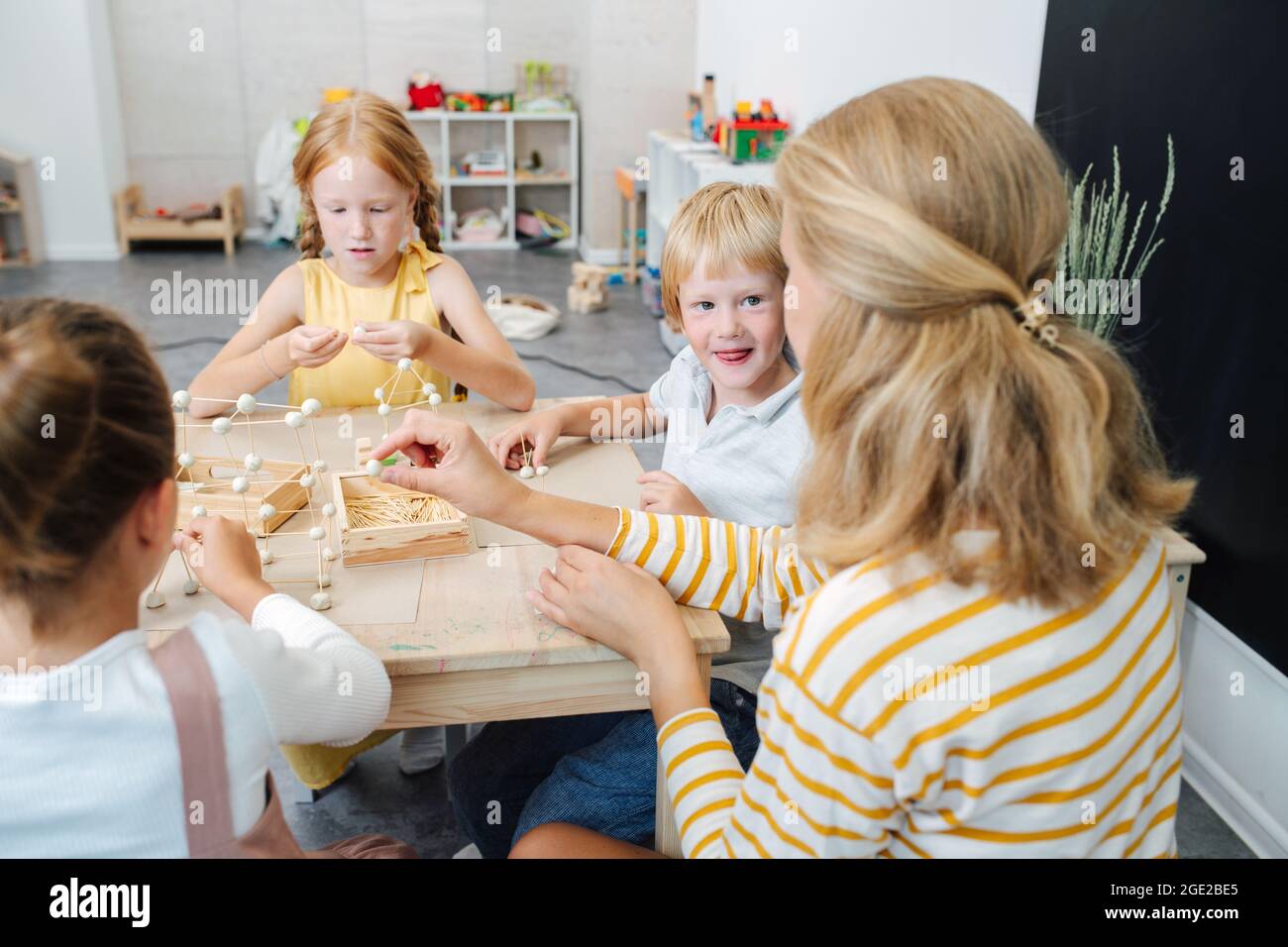 Female teacher helping kids to build 3d shapes from plasticine and ...