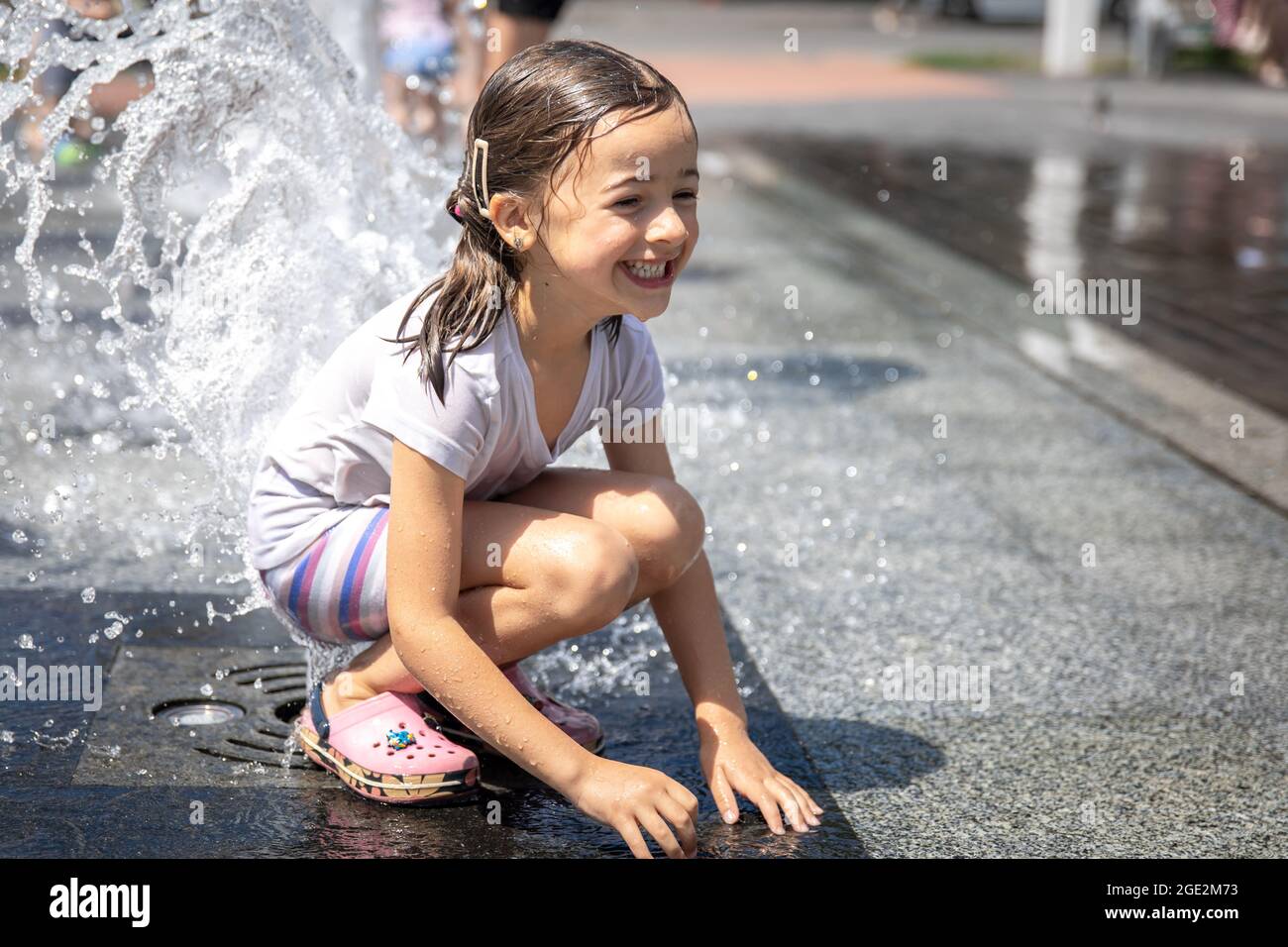 A little wet girl is cooling off in a fountain on a hot summer day ...