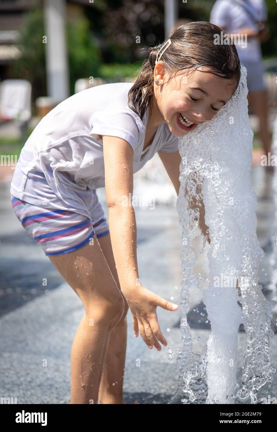 A little wet girl is cooling off in a fountain on a hot summer day ...