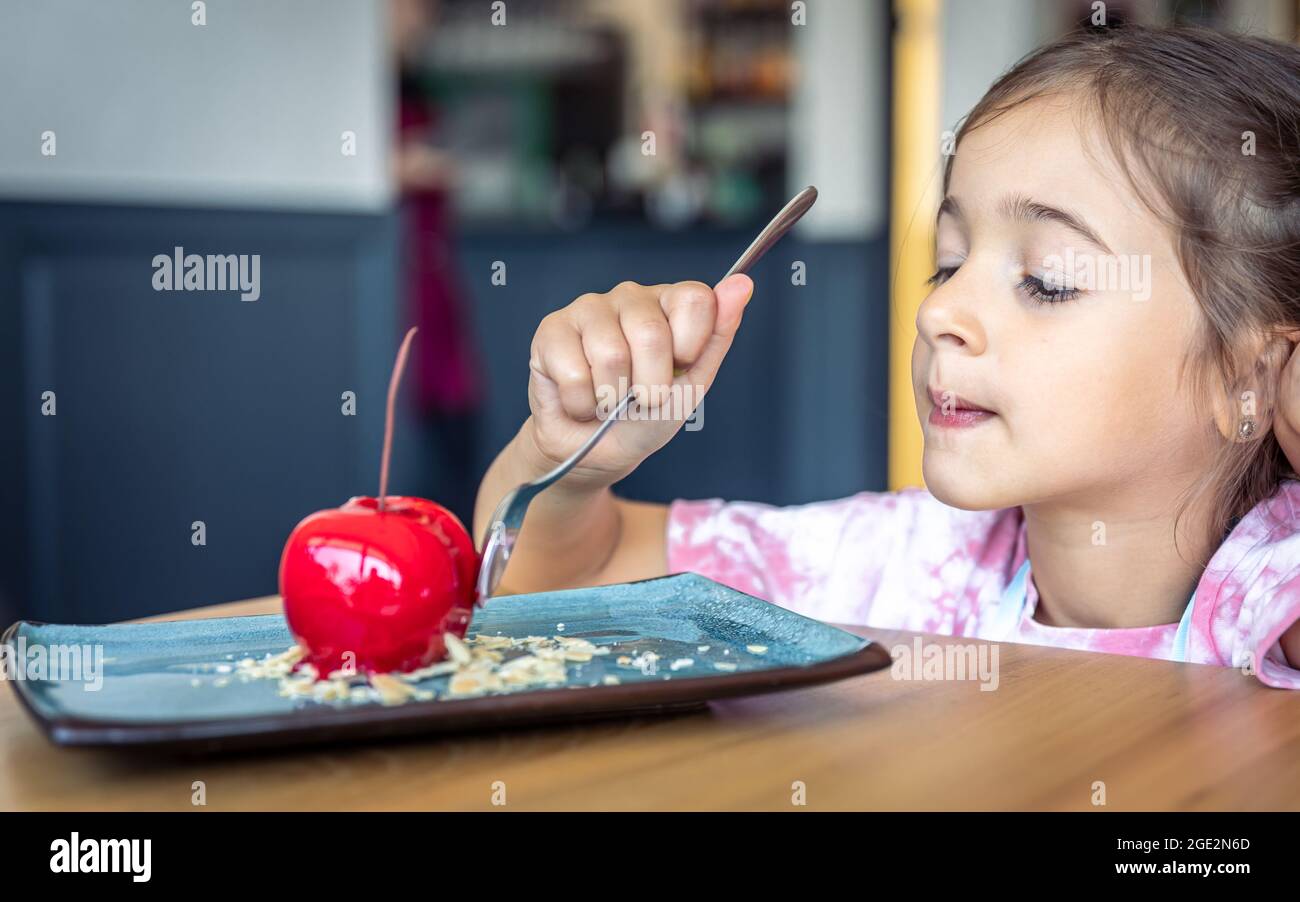 Cute little girl eating cherry-shaped chocolate mousse, french dessert ...