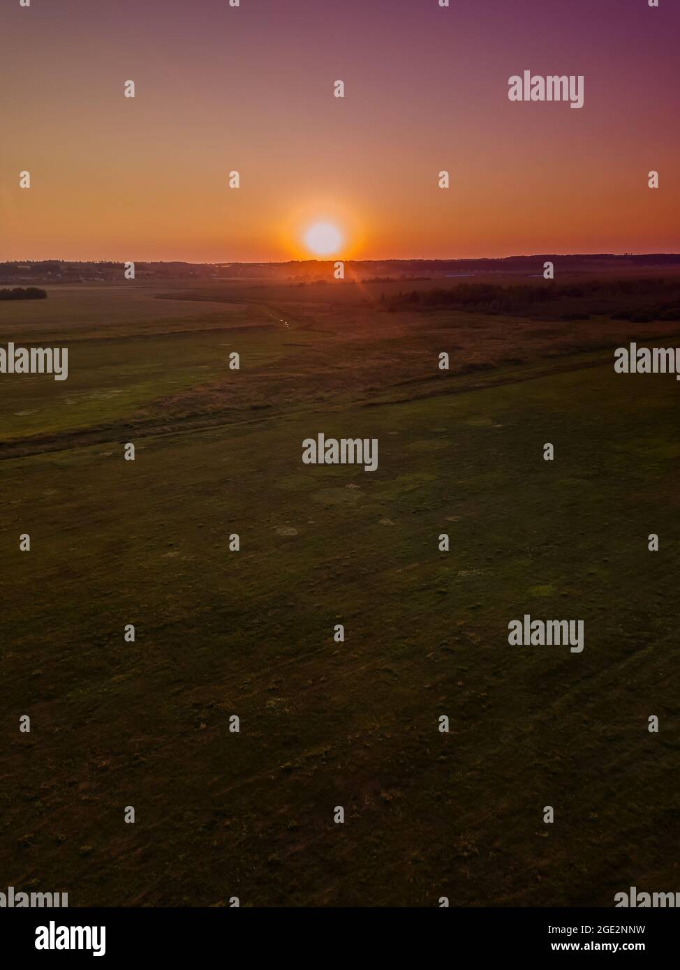 Bird's-eye view from above of a green field, forests in the distance ...