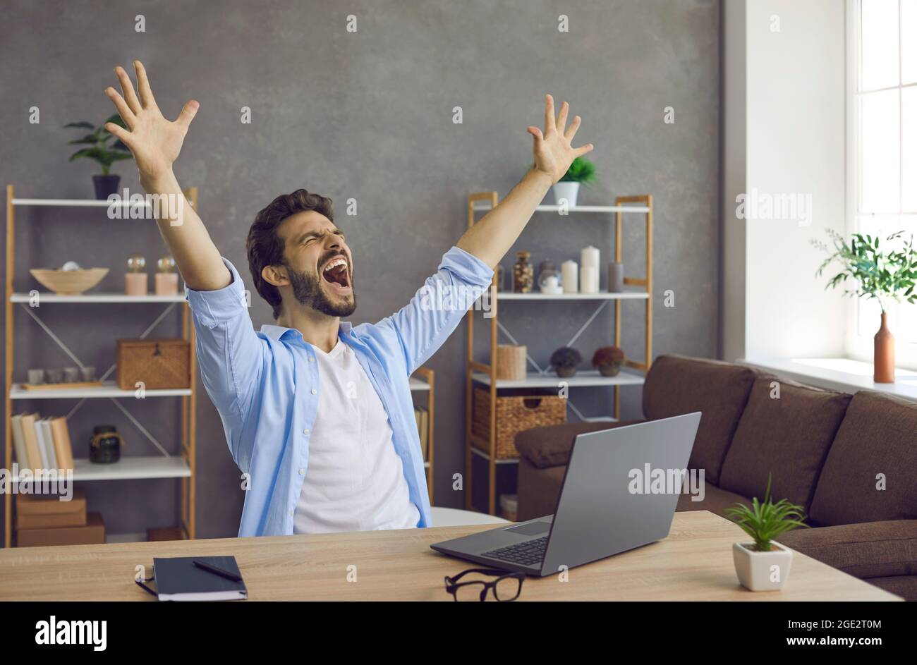Happy excited young man screaming sitting at his working desk with ...