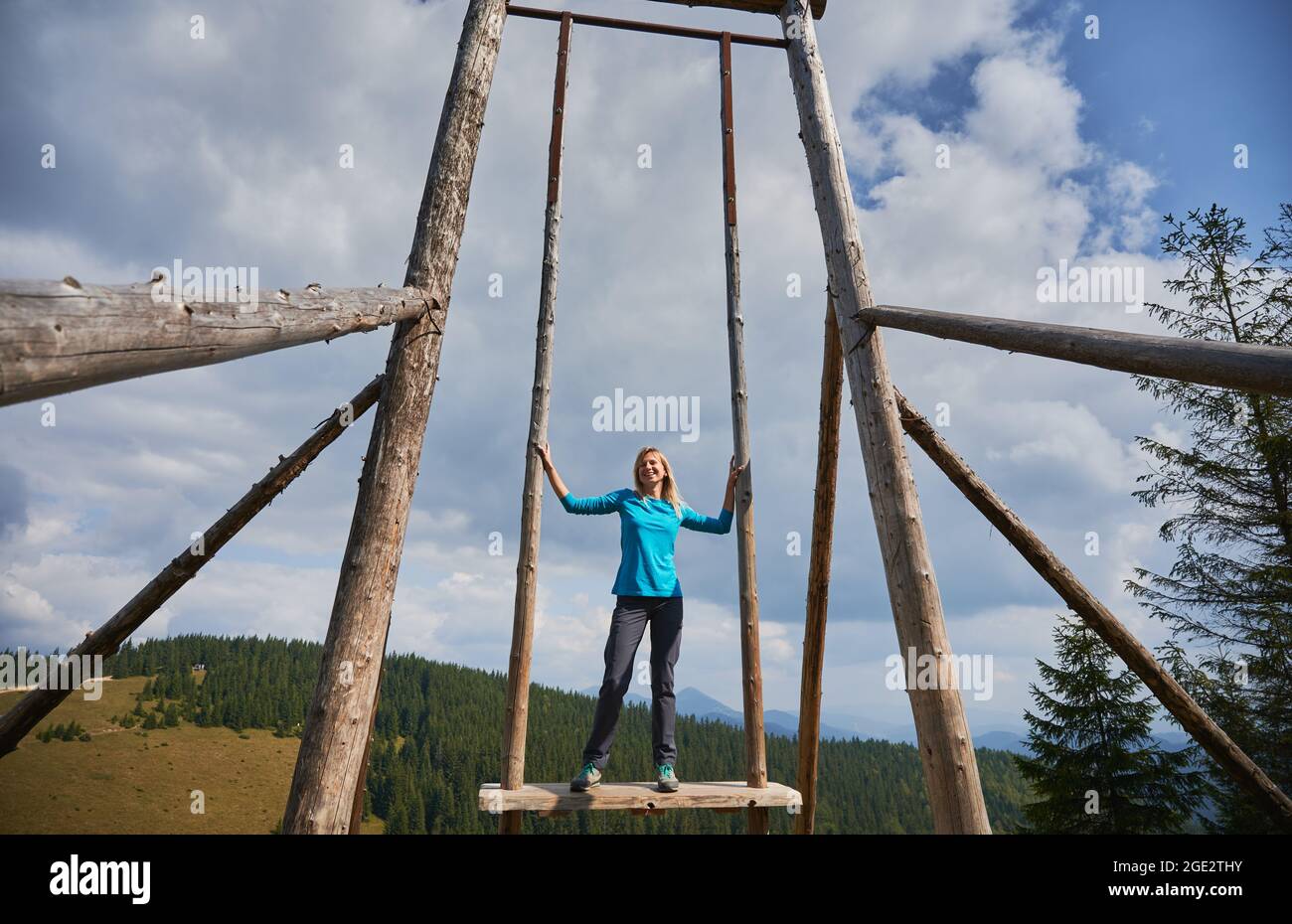 Slender blonde woman standing on seat of very large wooden frame swing ...