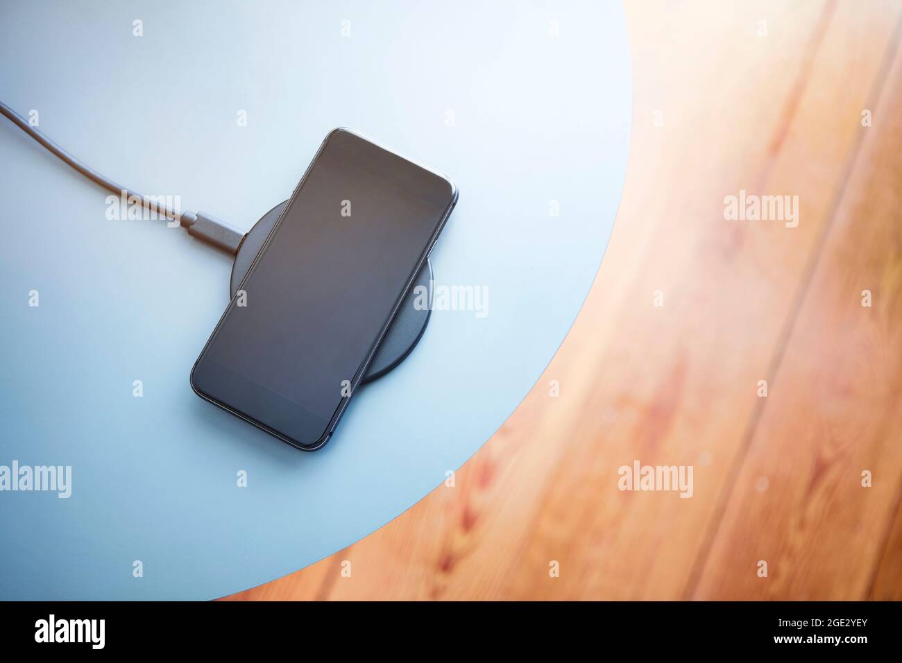 Top down view of smartphone lying on round charging pad. Light blue and ...