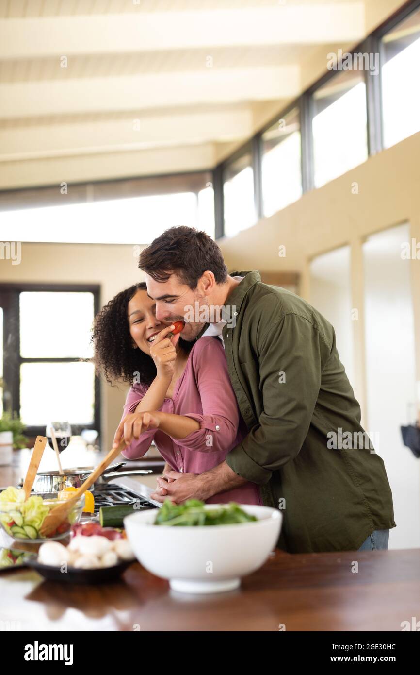 Happy diverse couple in kitchen preparing food together eating and ...