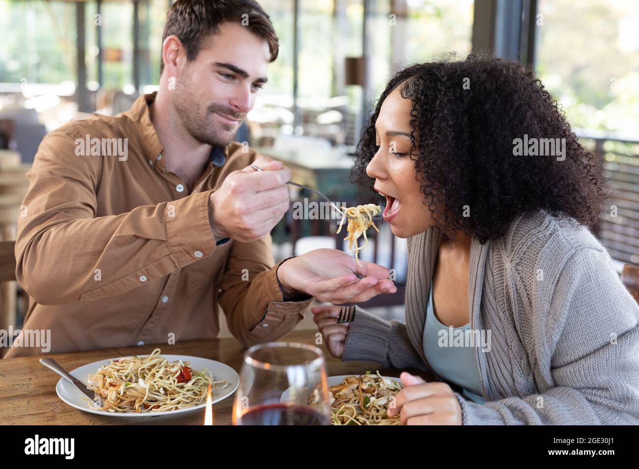 Happy diverse couple in living room sitting at table eating dinner ...