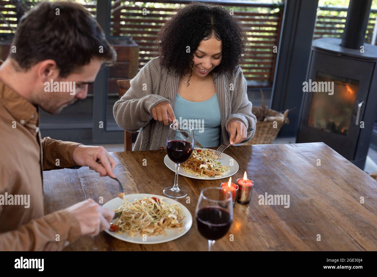 Happy diverse couple in living room sitting at table eating dinner ...