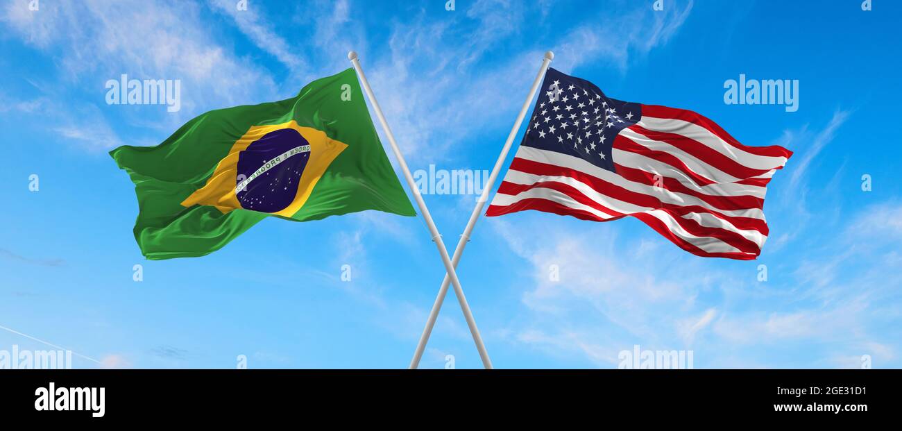 flags of USA and Brazil waving in the wind on flagpoles against the sky ...