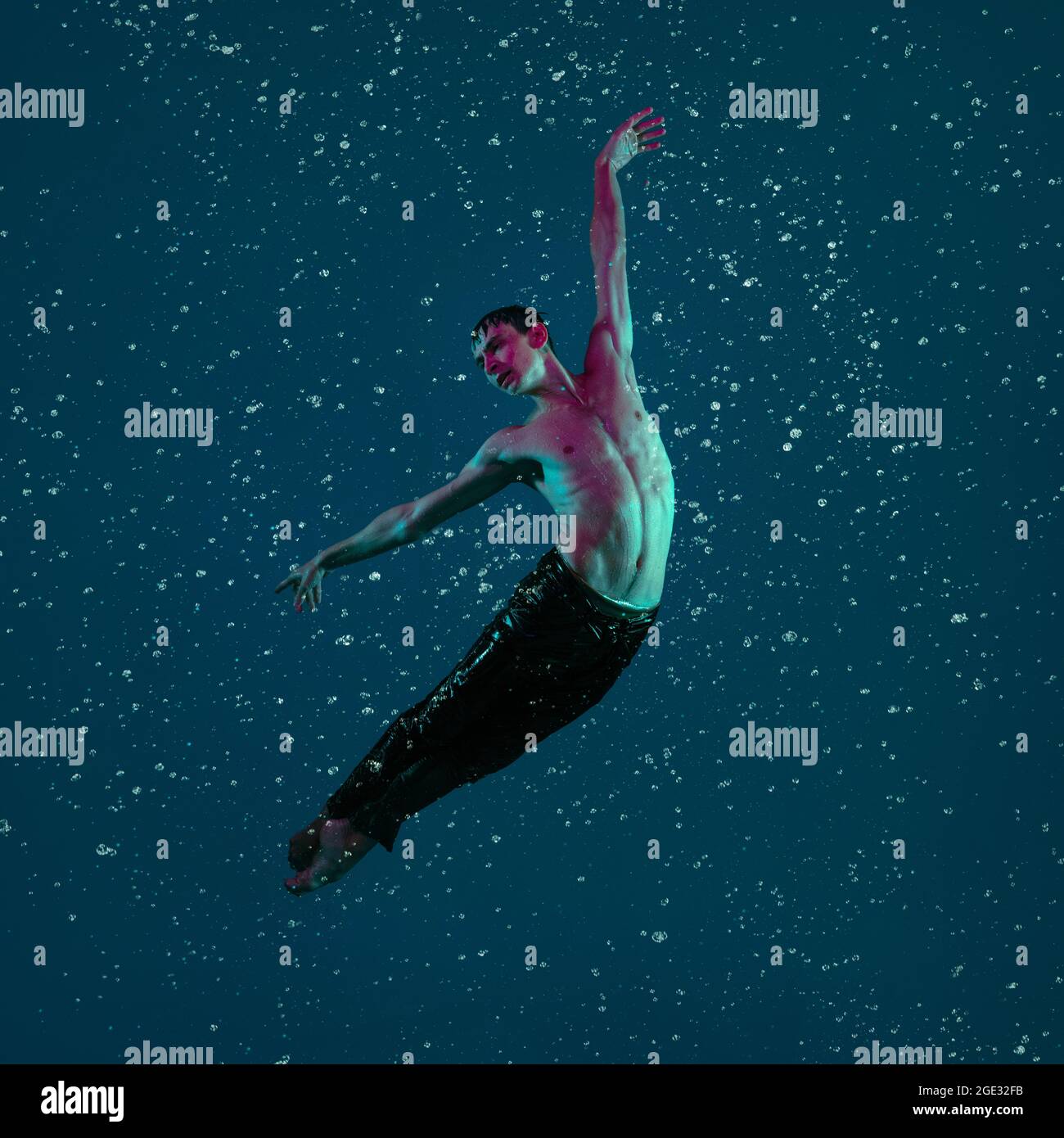 One young male ballet dancer in motion, action under the rain over blue ...