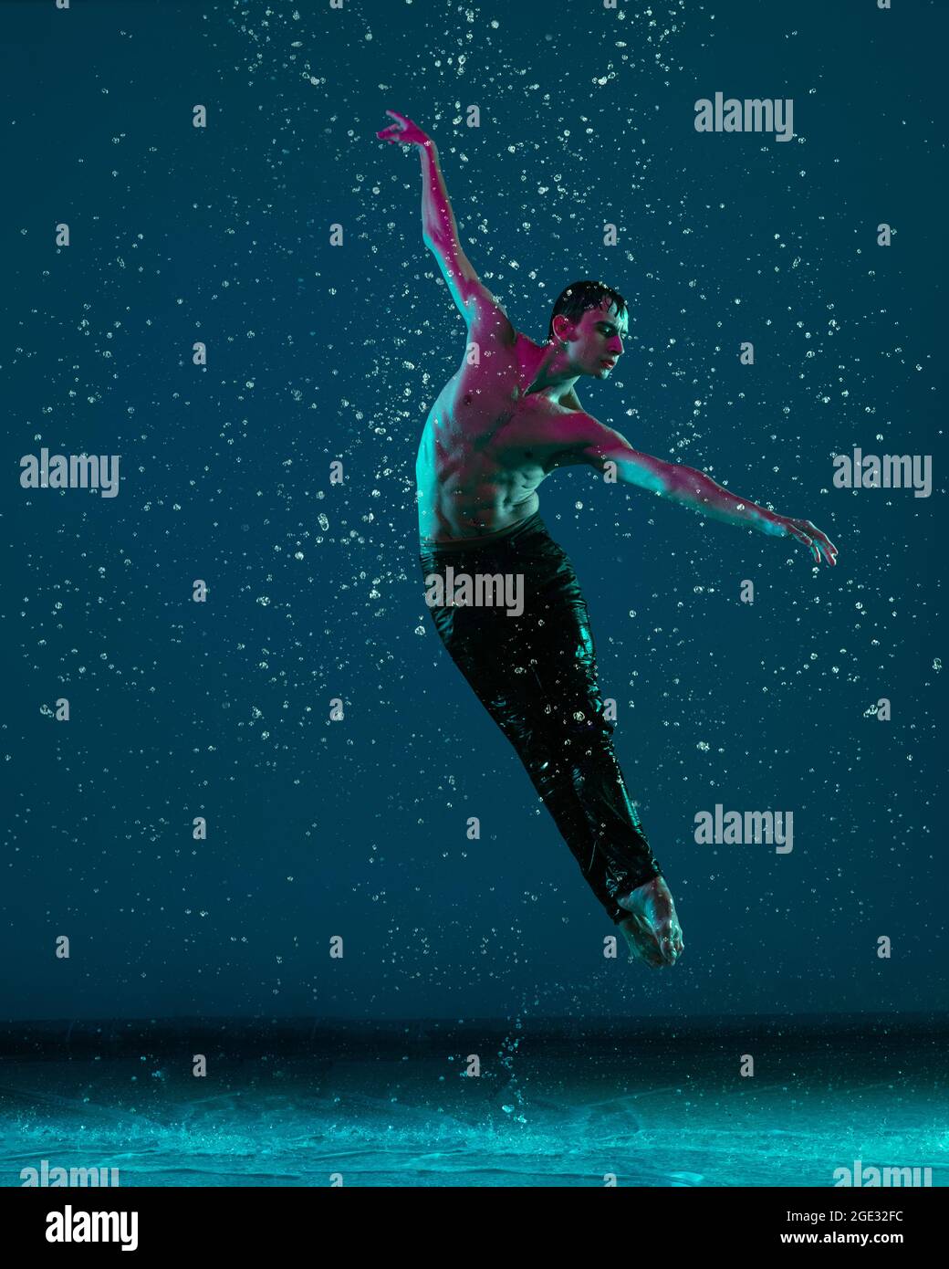 One young male ballet dancer in motion, action under the rain over blue ...