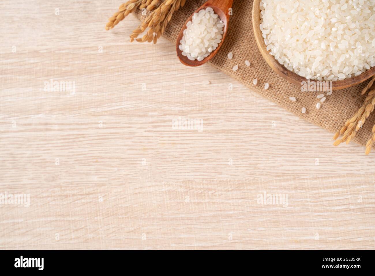 White raw rice in a bowl with the ear on the wooden table background ...