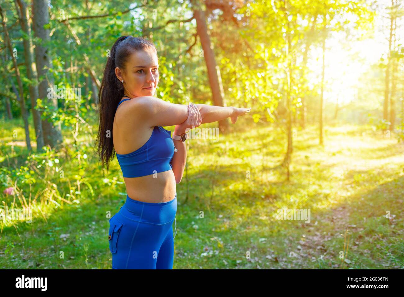 Woman runner stretching arms before exercising in a summer park morning ...