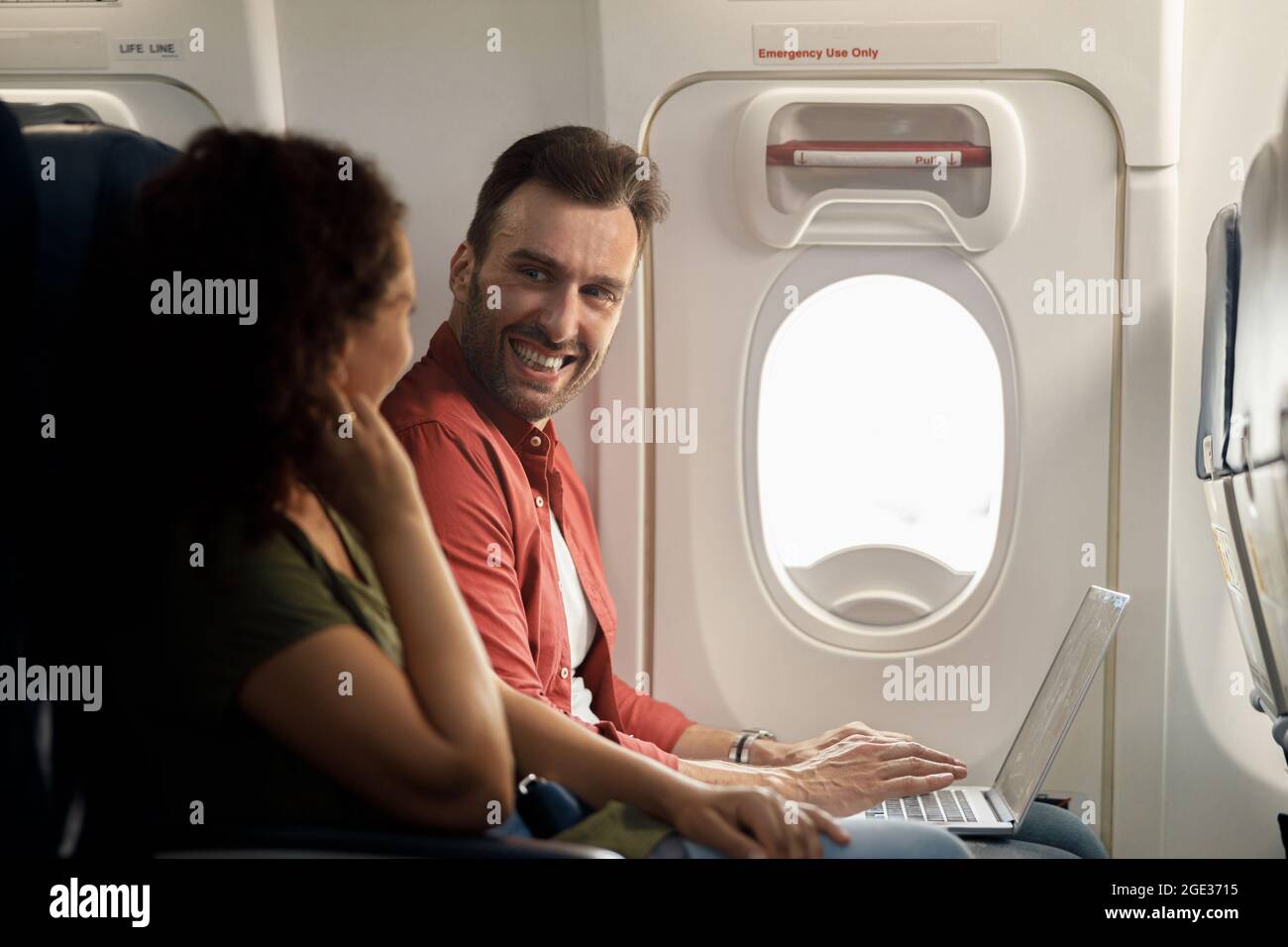 Cheerful caucasian man smiling to his wife while using laptop computer ...