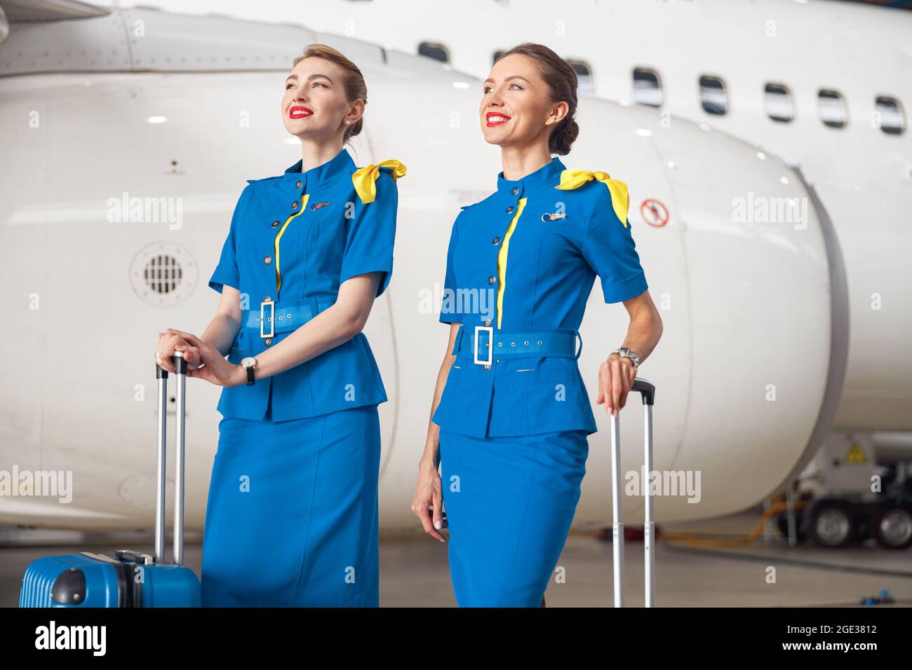 Two confident air stewardesses in bright blue uniform standing with ...