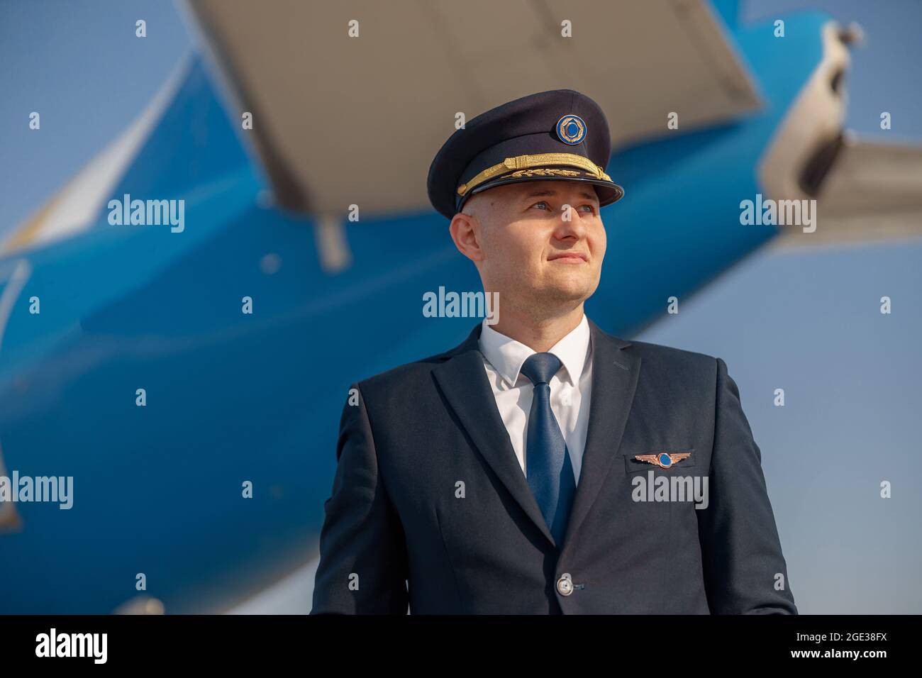 Portrait of pilot in uniform looking away, standing in front of big ...