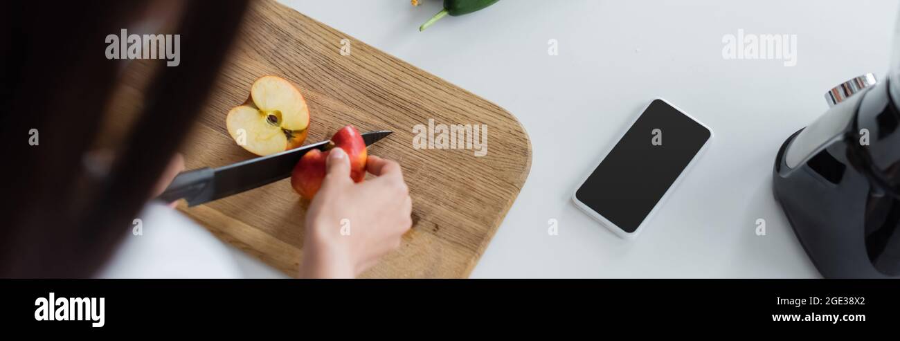 cropped view of blurred woman cutting ripe apple near smartphone with ...