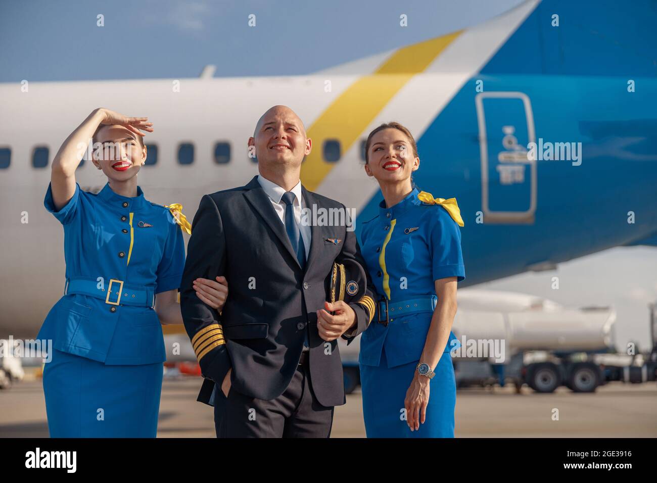 Happy pilot and two pretty stewardesses standing together in front of ...