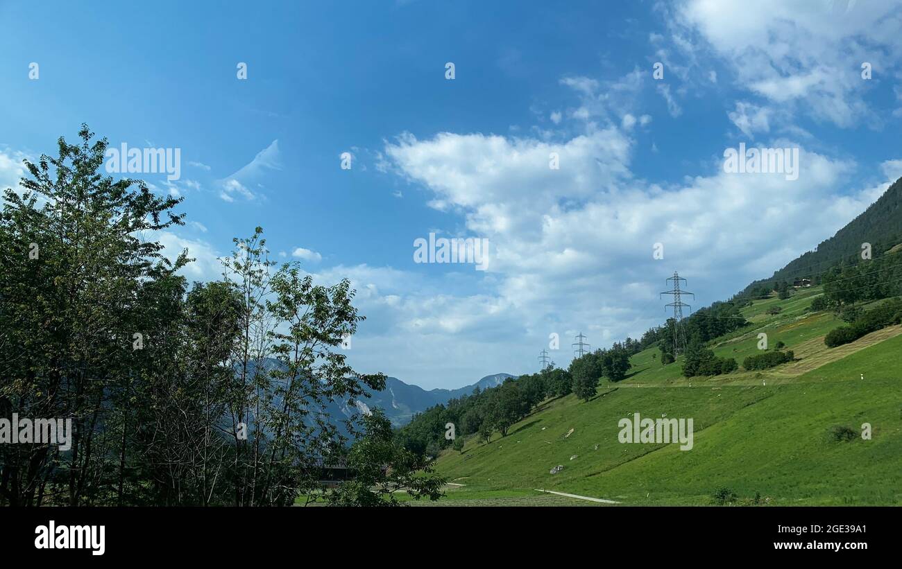 Green slope of the Swiss Alps with pylons and trees against a blue ...