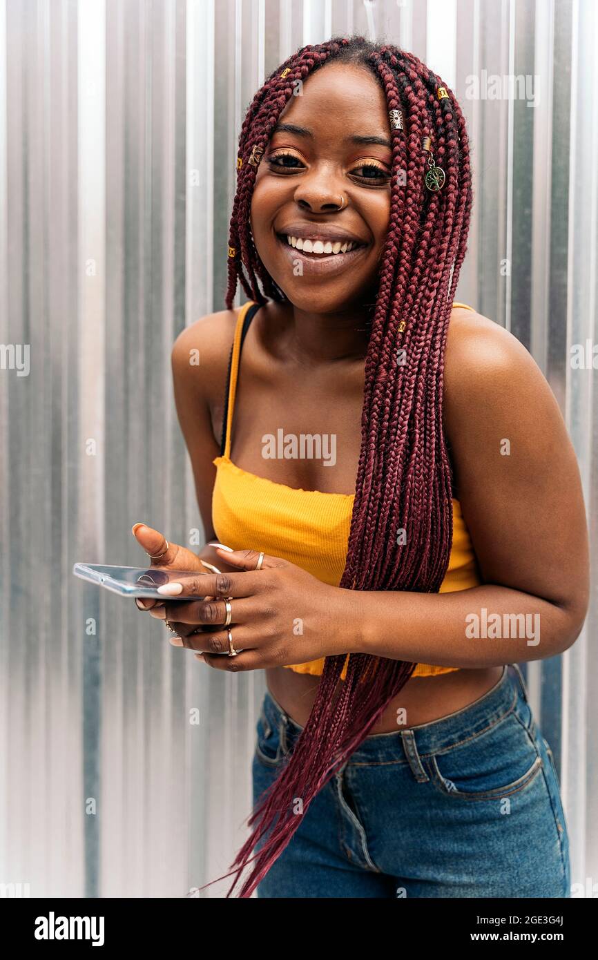 Cheerful young african woman with braids looking at camera and holding ...