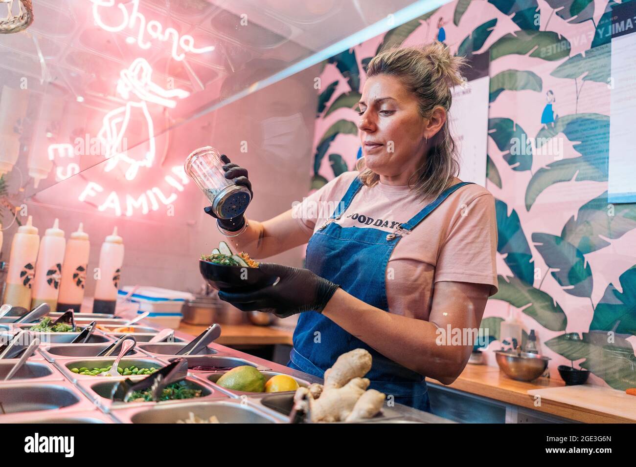 Focused restaurant worker wearing apron preparing poke bowl and adding ...