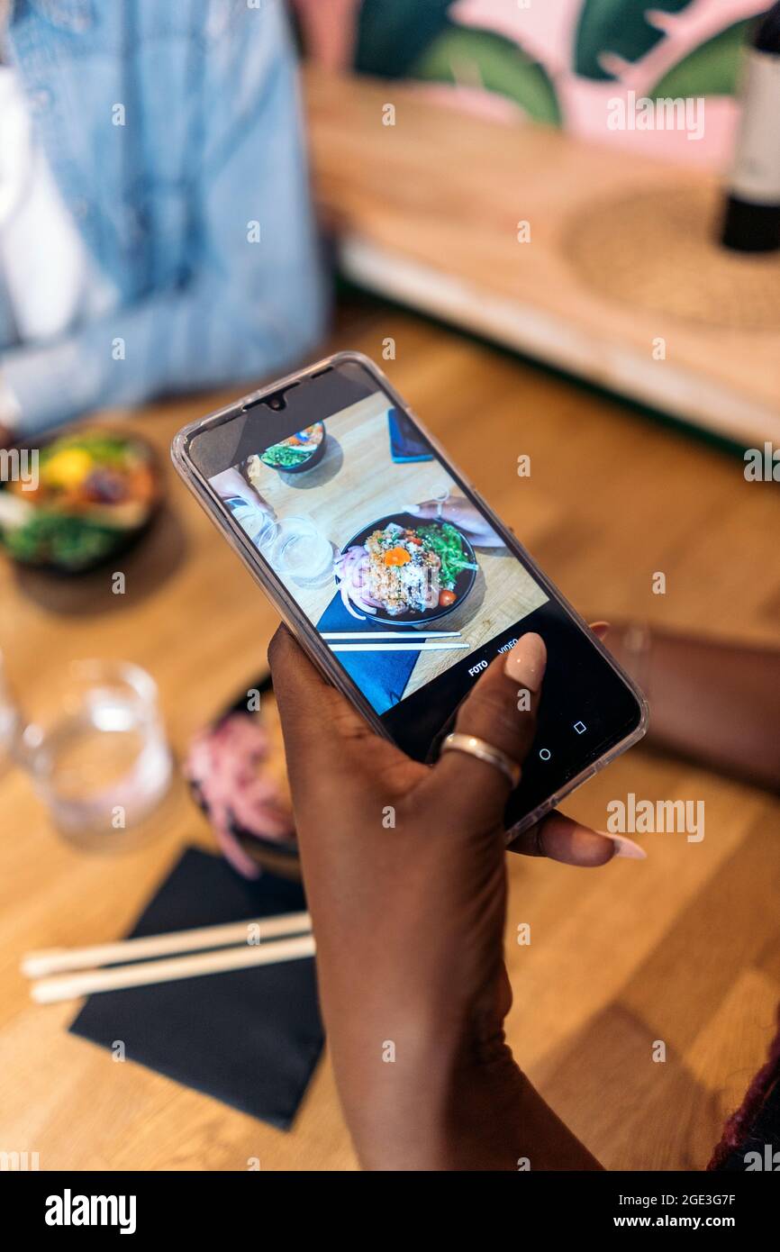 Unrecognized african woman taking a photo of her poke bowl in a ...