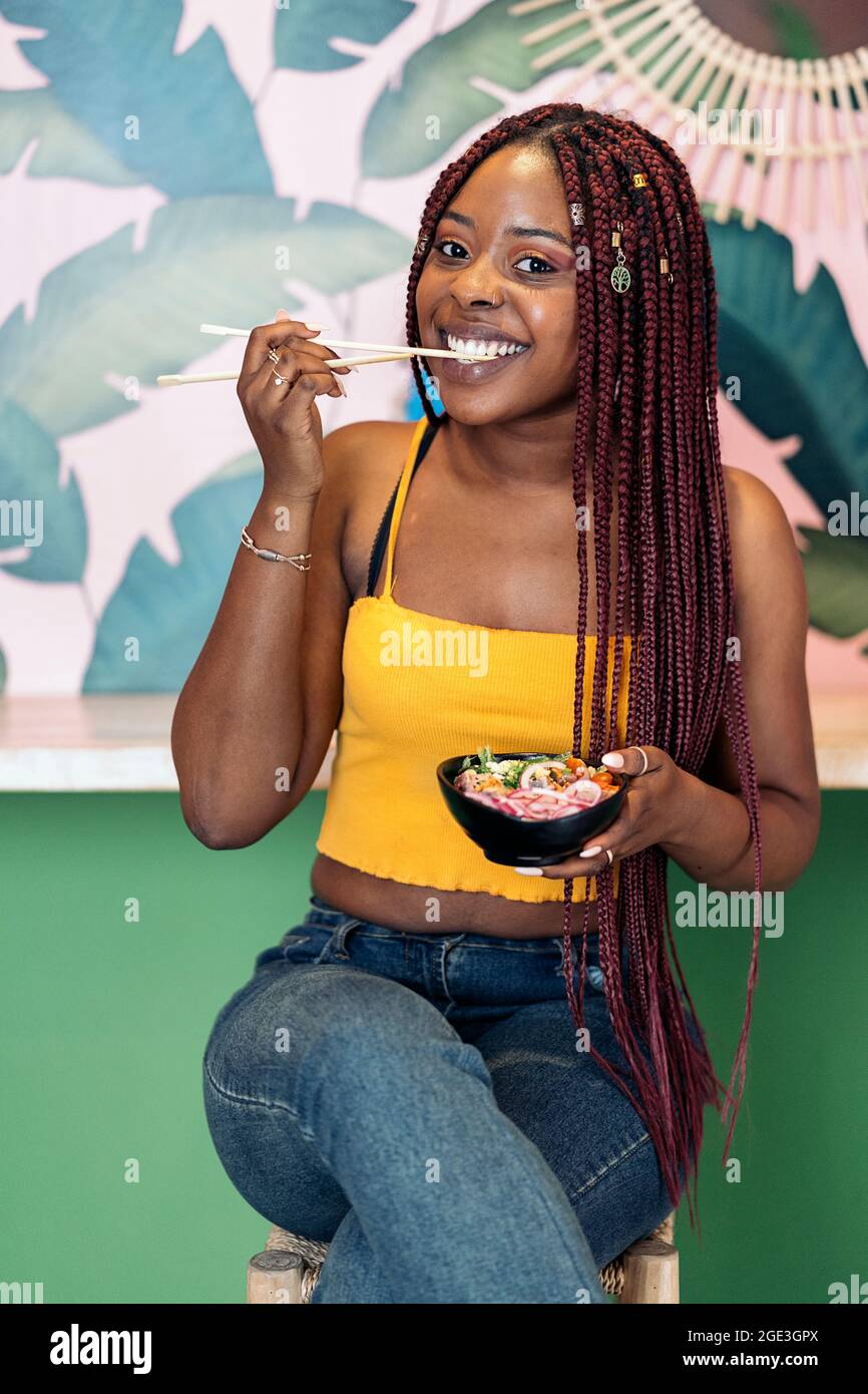 Cheerful african woman sitting in a restaurant enjoying a healthy poke ...