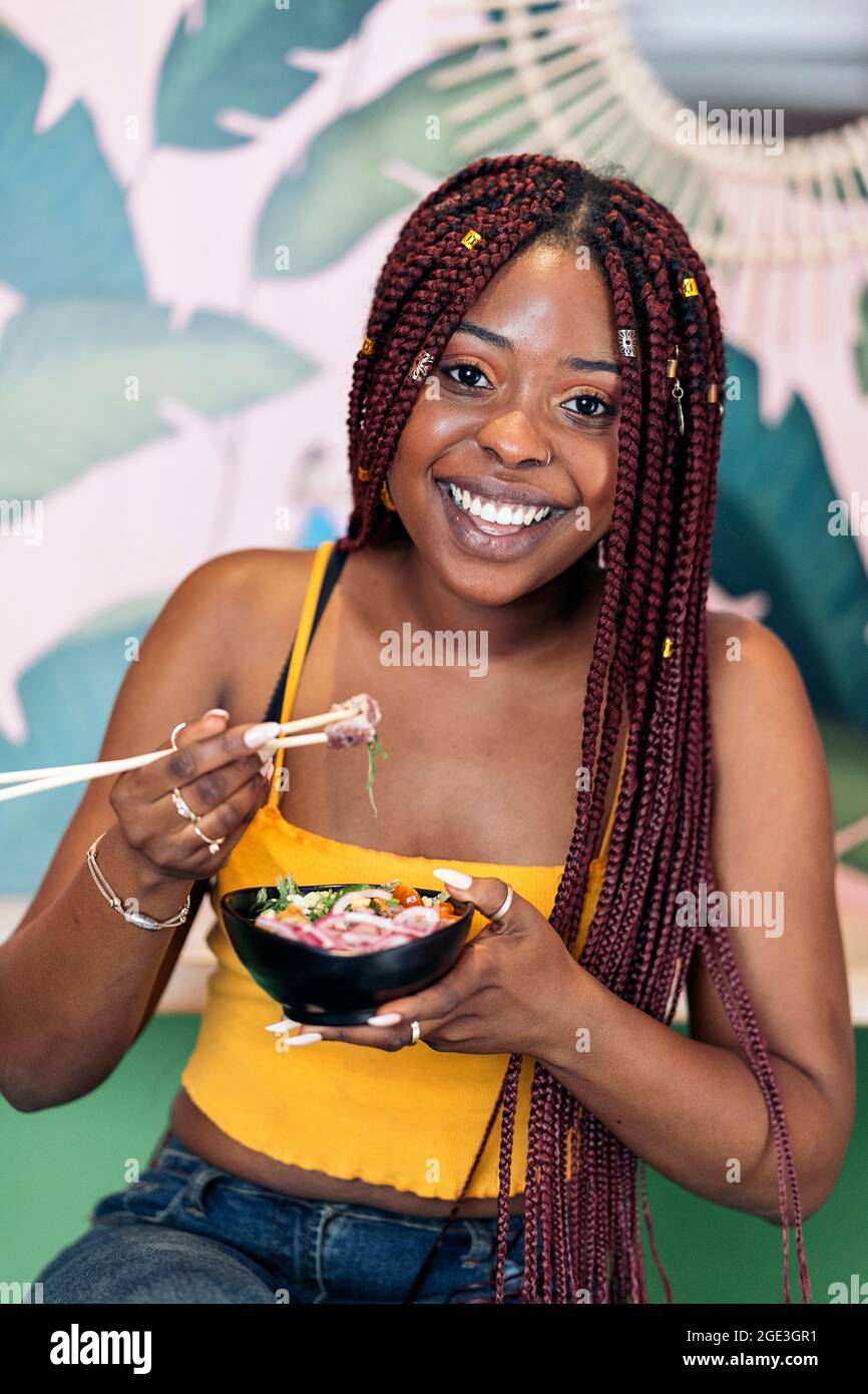 Cheerful african woman sitting in a restaurant enjoying a healthy poke ...
