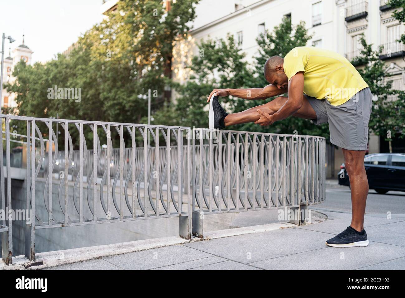 African American man stretching his right leg over railing in the city ...