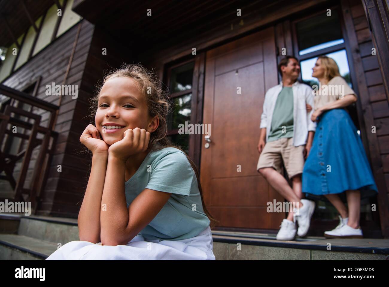 Girl looking at camera on stairs near blurred parents and vacation ...