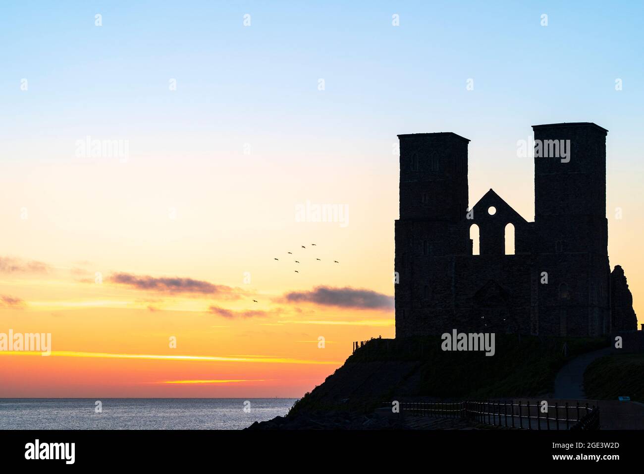 The dawn sky with a small flock of birds flying over the sea and the ...