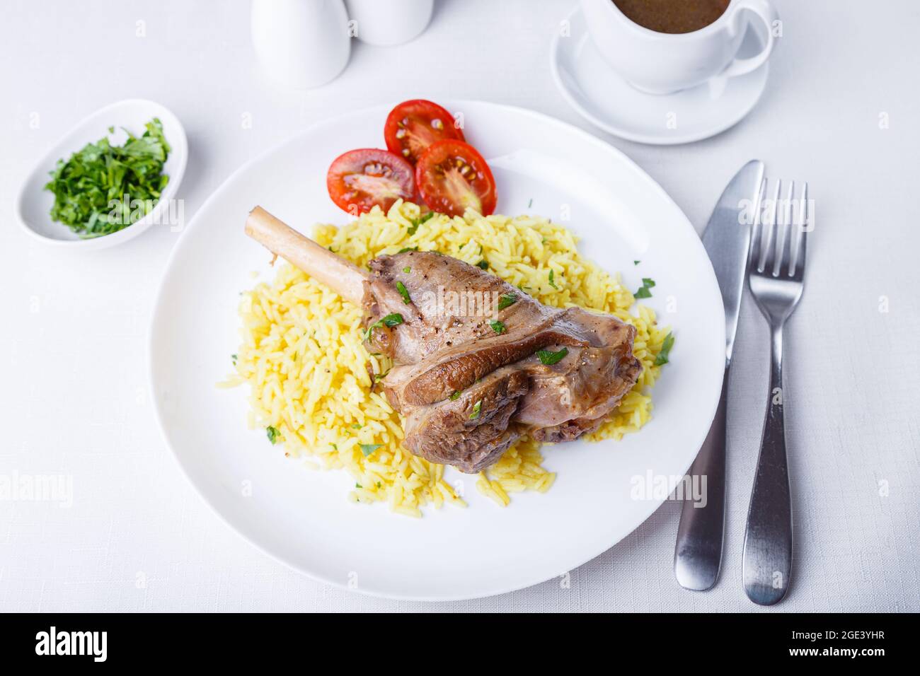 Lamb shin (shank) with rice, parsley, tomatoes and sauce on a white ...