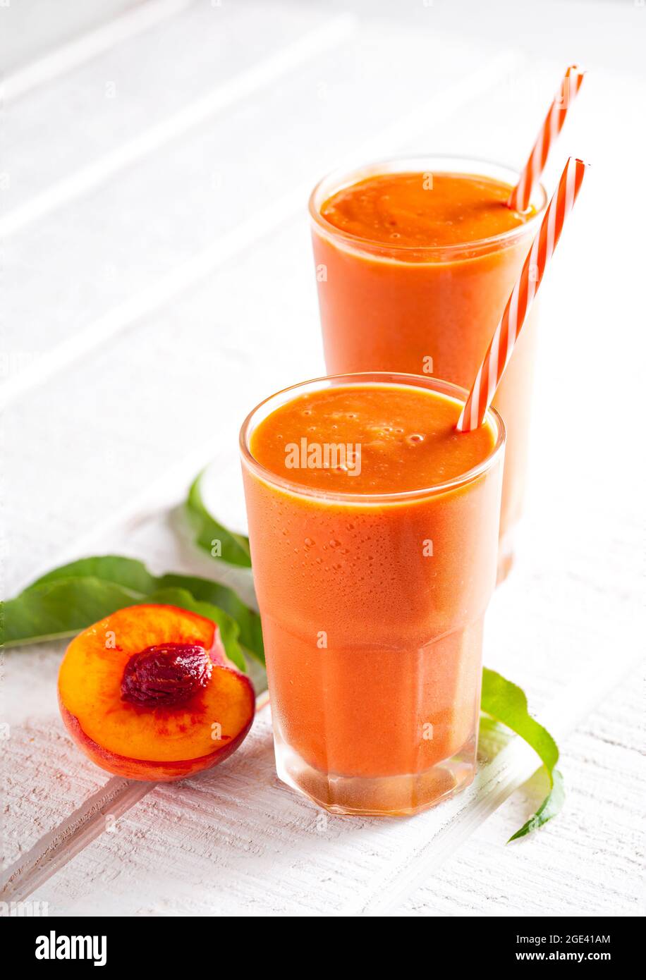 Two fresh yellow peach smoothies on a bright wooden surface with copy ...