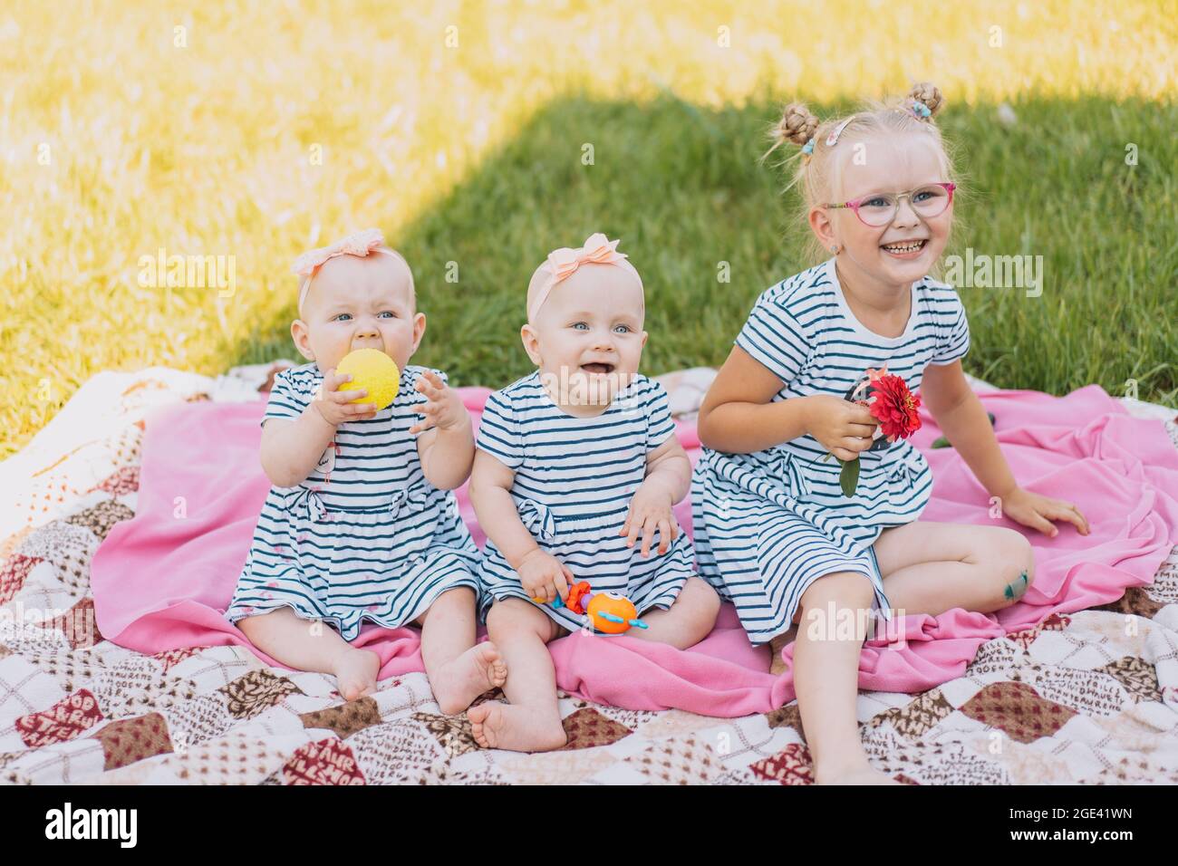 Three sisters in striped dresses are resting in the park on the grass ...