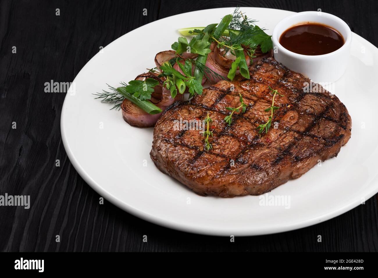 Grilled black angus steak ribeye on white plate on black wooden ...