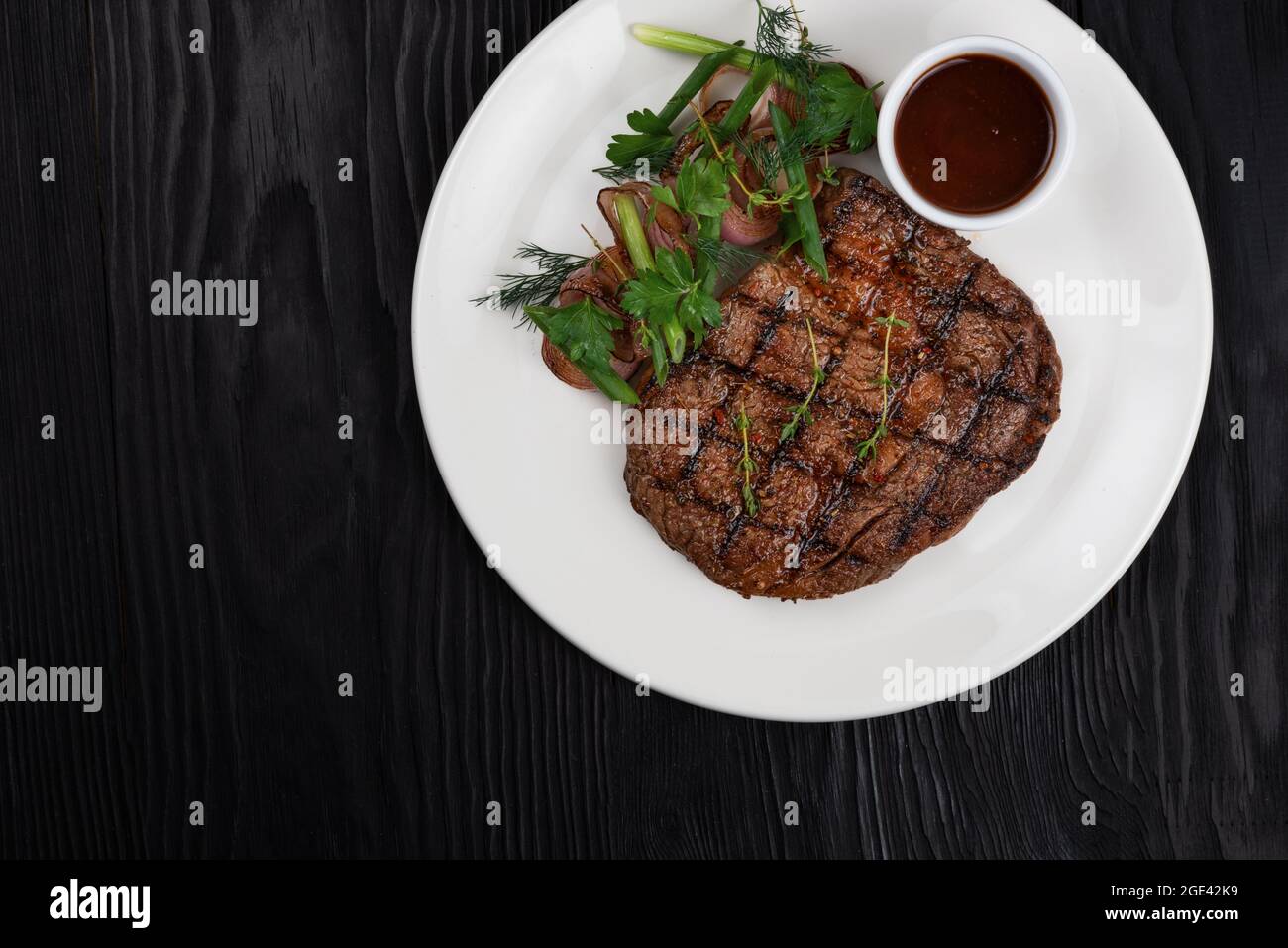 Grilled black angus steak ribeye on white plate on black wooden ...