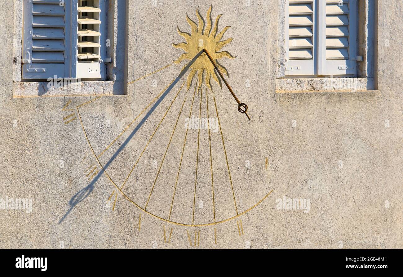 Closeup view of a sun clock on the wall with the windows of the ...
