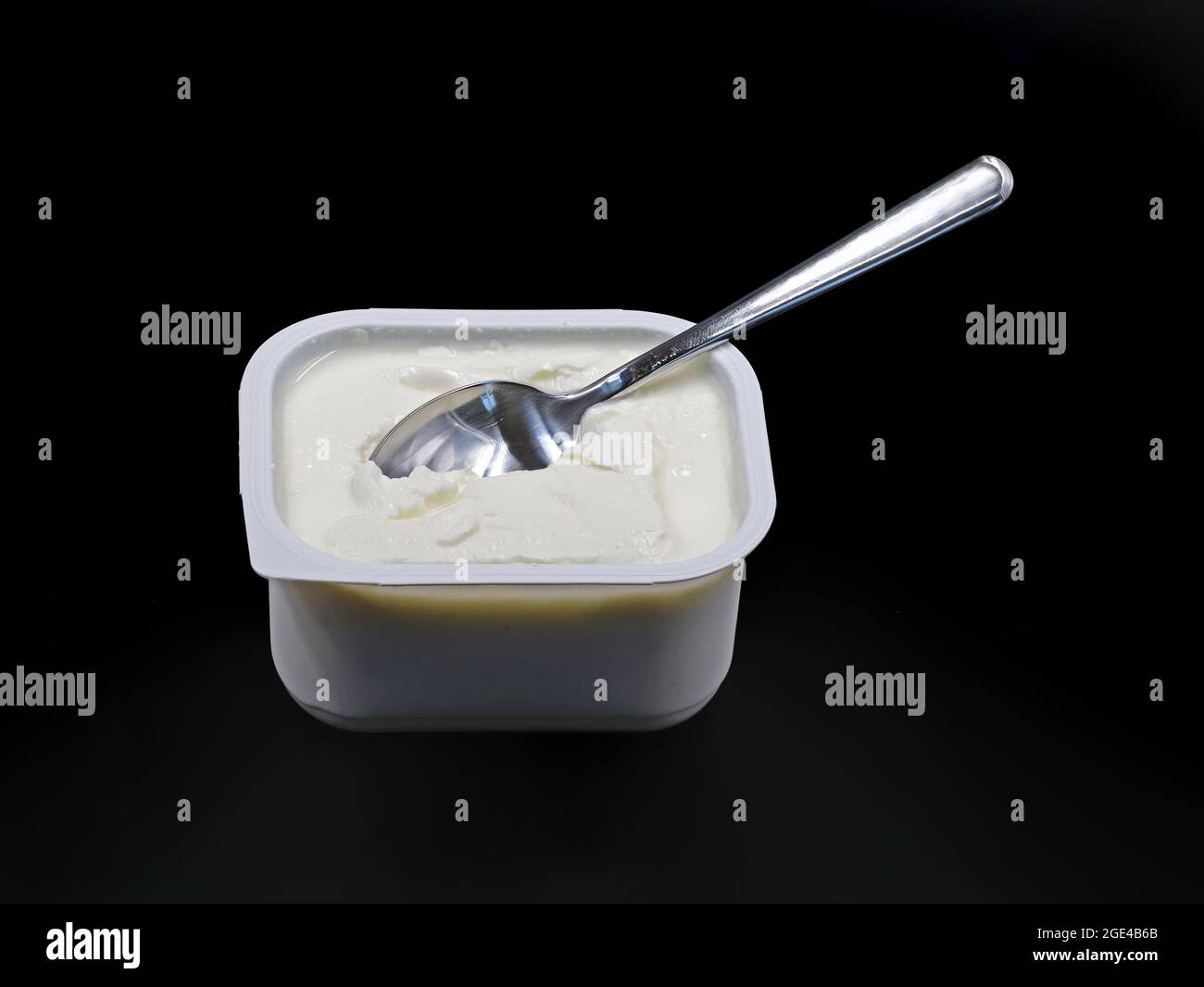 low-fat quark in plastic container with spoon isolated on black ...