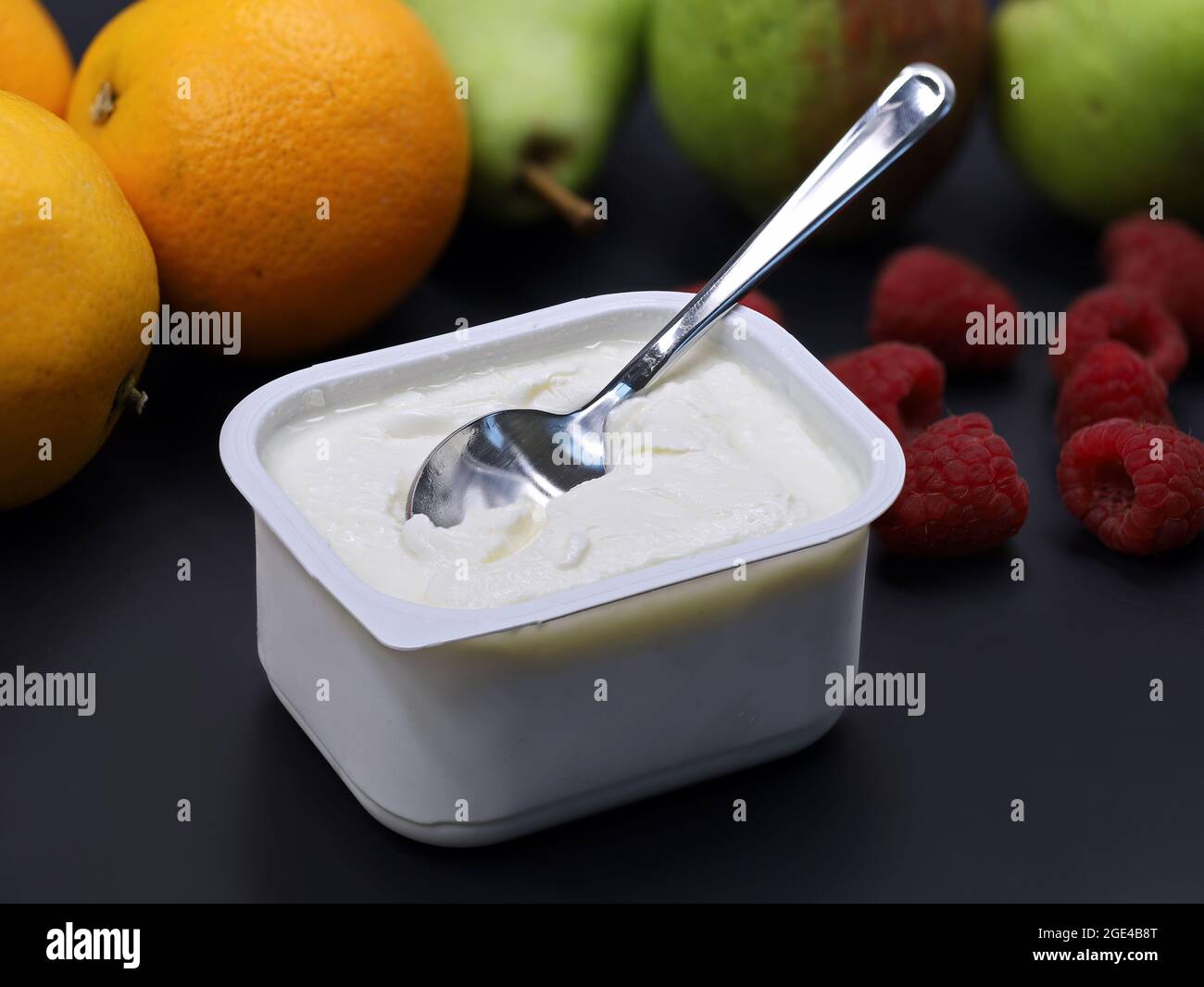 quark or cream cheese in plastic box with spoon on black backround with ...