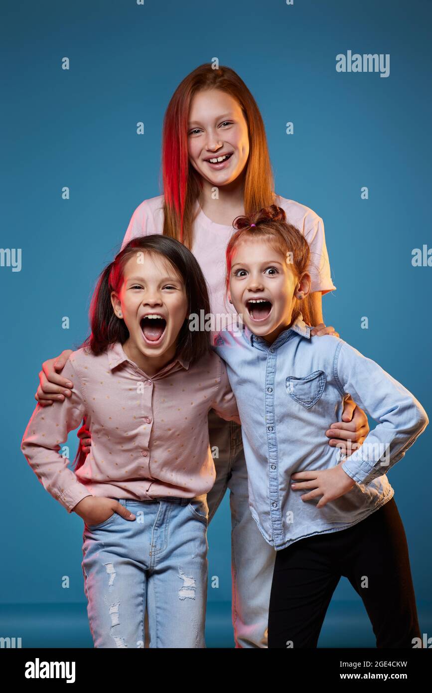 three kids girls standing together on blue background Stock Photo - Alamy