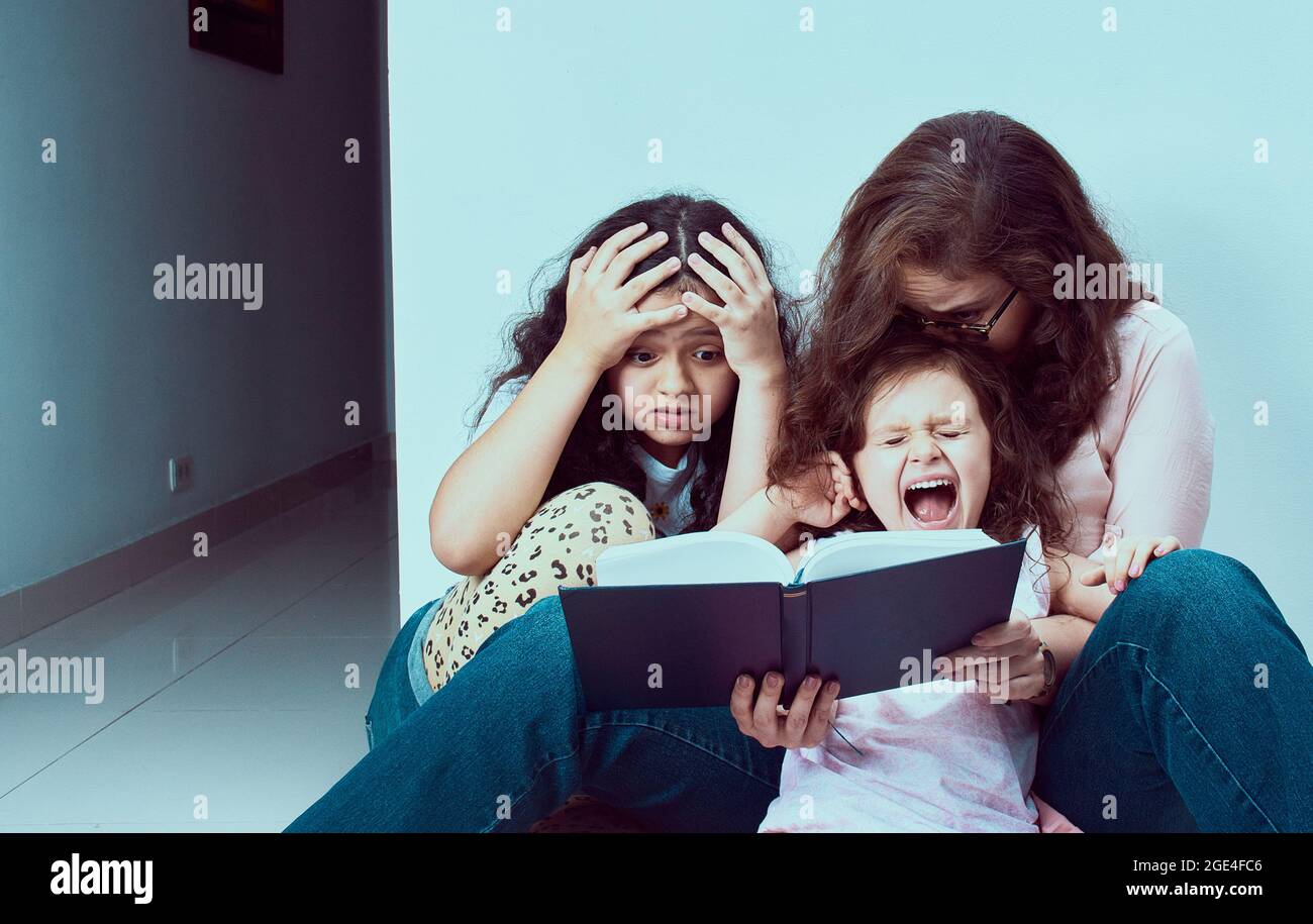 Girls with terrified looks while reading a book with their mother Stock ...