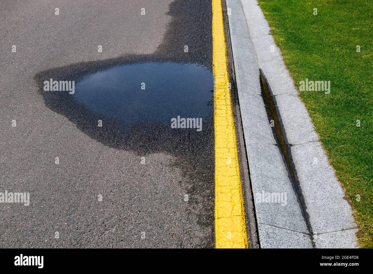 puddle on asphalt road with stormwater on the road side with a ditch ...