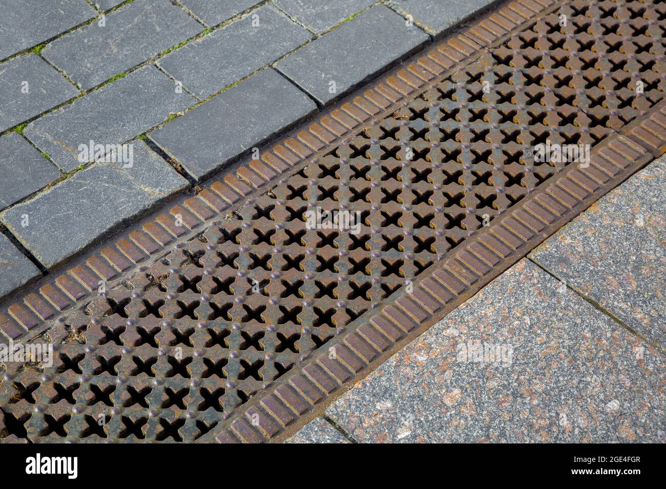 a drainage ditch covered with an iron patterned lattice on a sidewalk ...