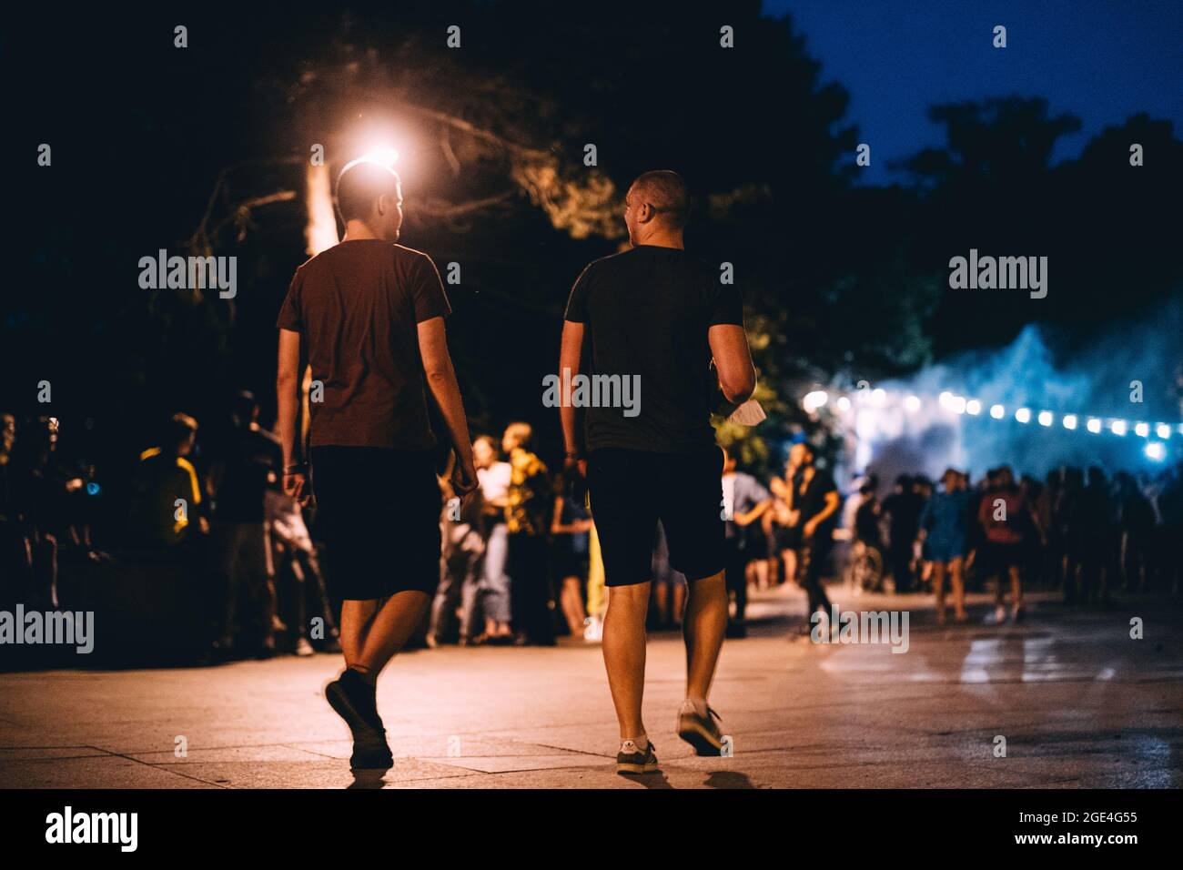 Two young men walking in a crowded park at night Stock Photo - Alamy