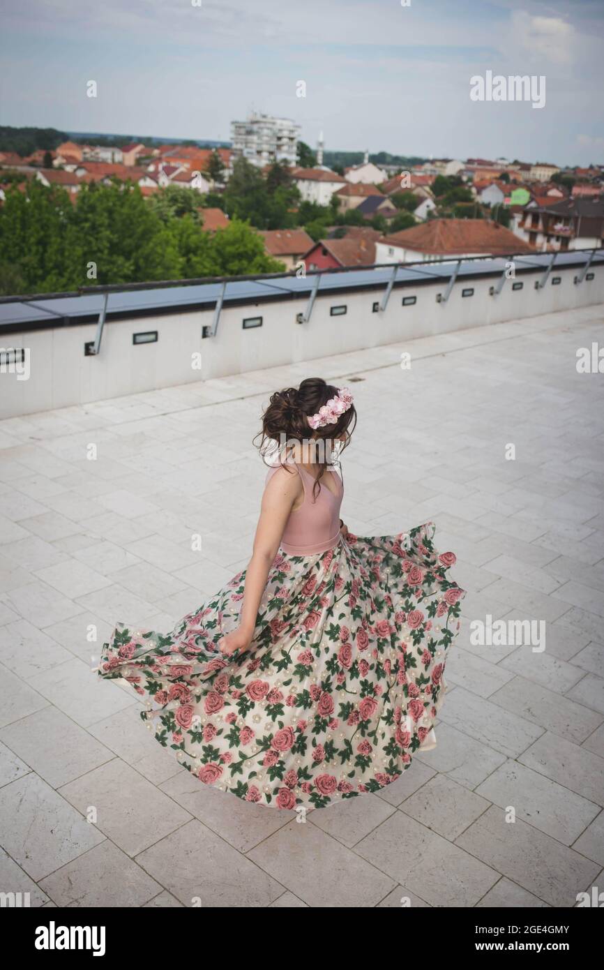 Vertical shot of a woman rotating on a building roof in a pink dress ...