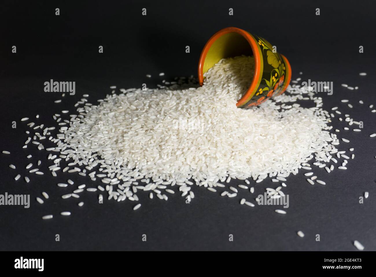 Scattered rice uncooked grains with painted wooden cup on a black ...