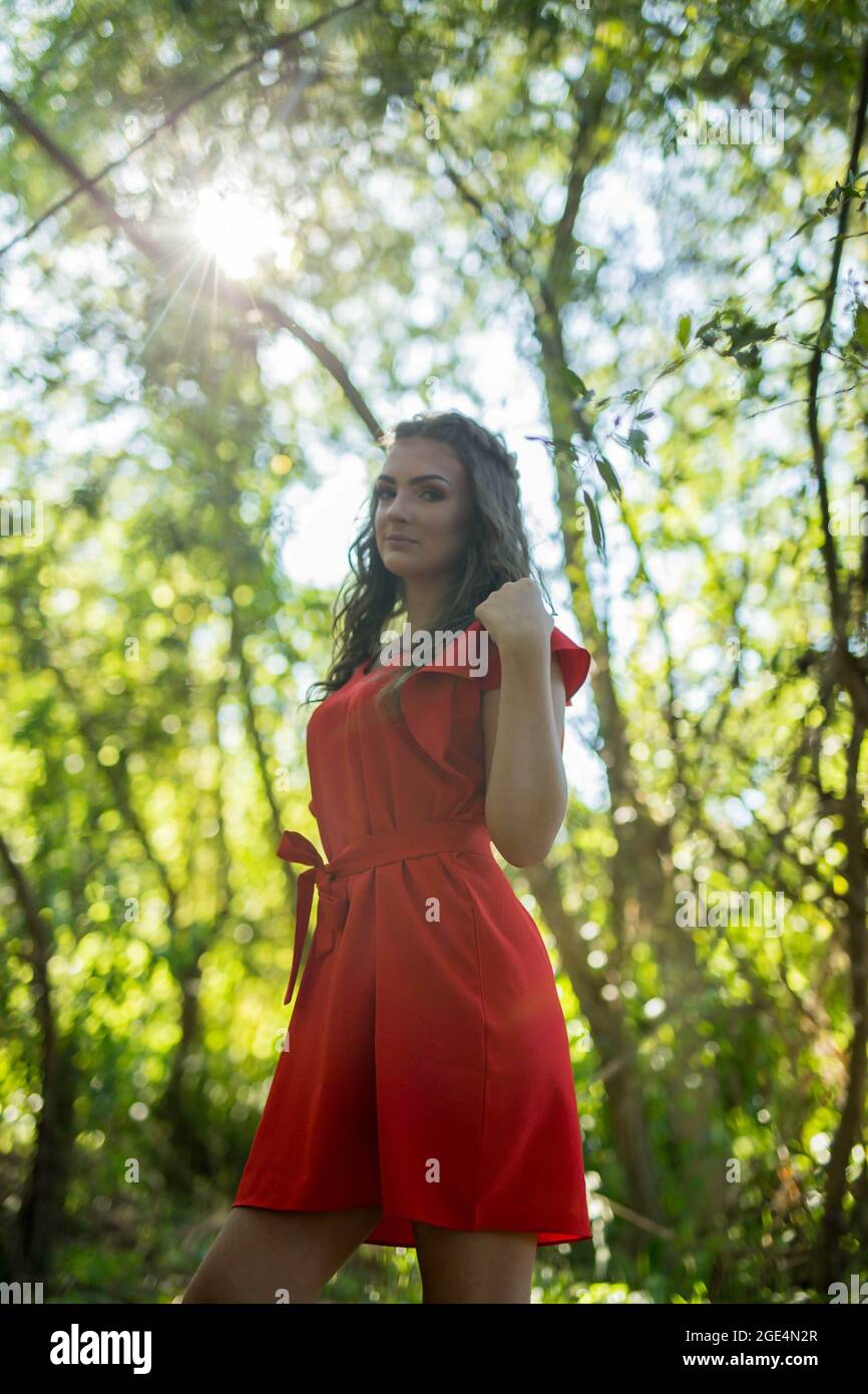 Shallow focus shot of a young woman standing outdoors in a red dress ...